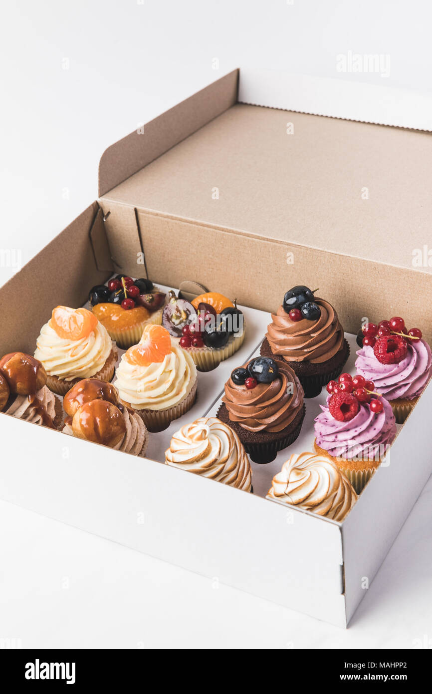 close up view of various types of cupcakes in cardboard box isolated on ...