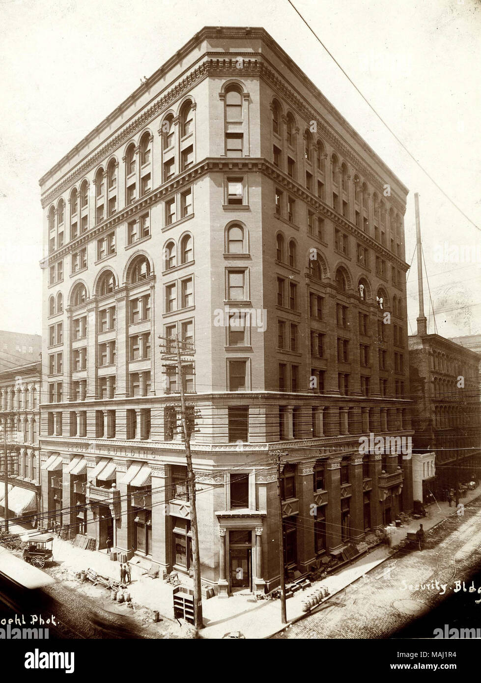 Vertical photograph of a tall building on a street corner. Awnings over ...
