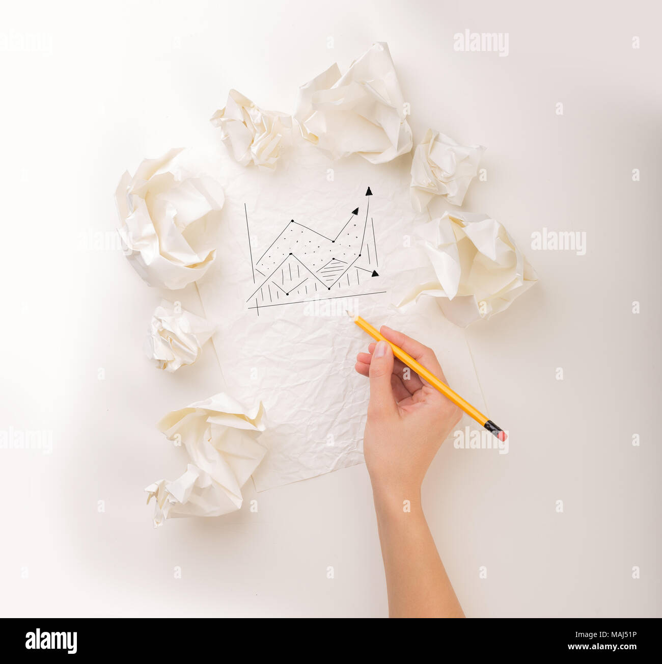 Female hand next to a few crumpled paper balls drawing a progress chart ...