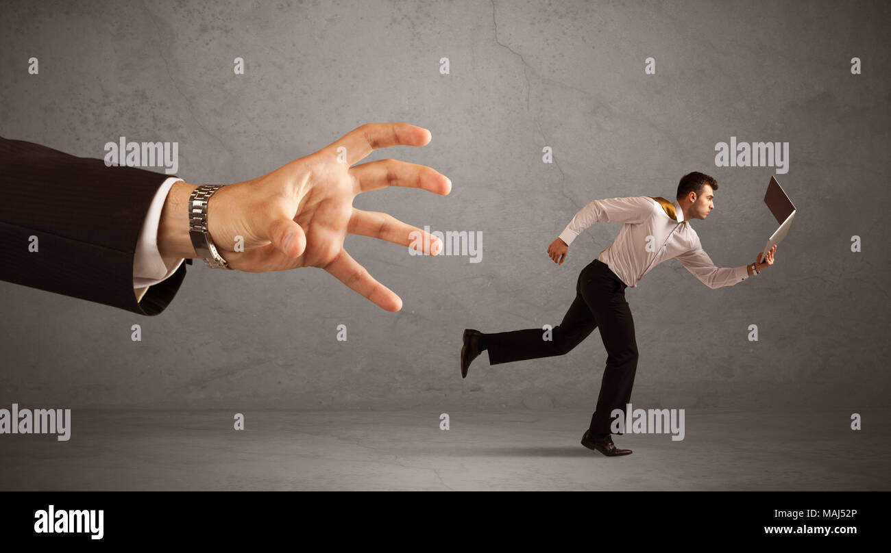 Young miniature businessman running from a big hand with grey ...