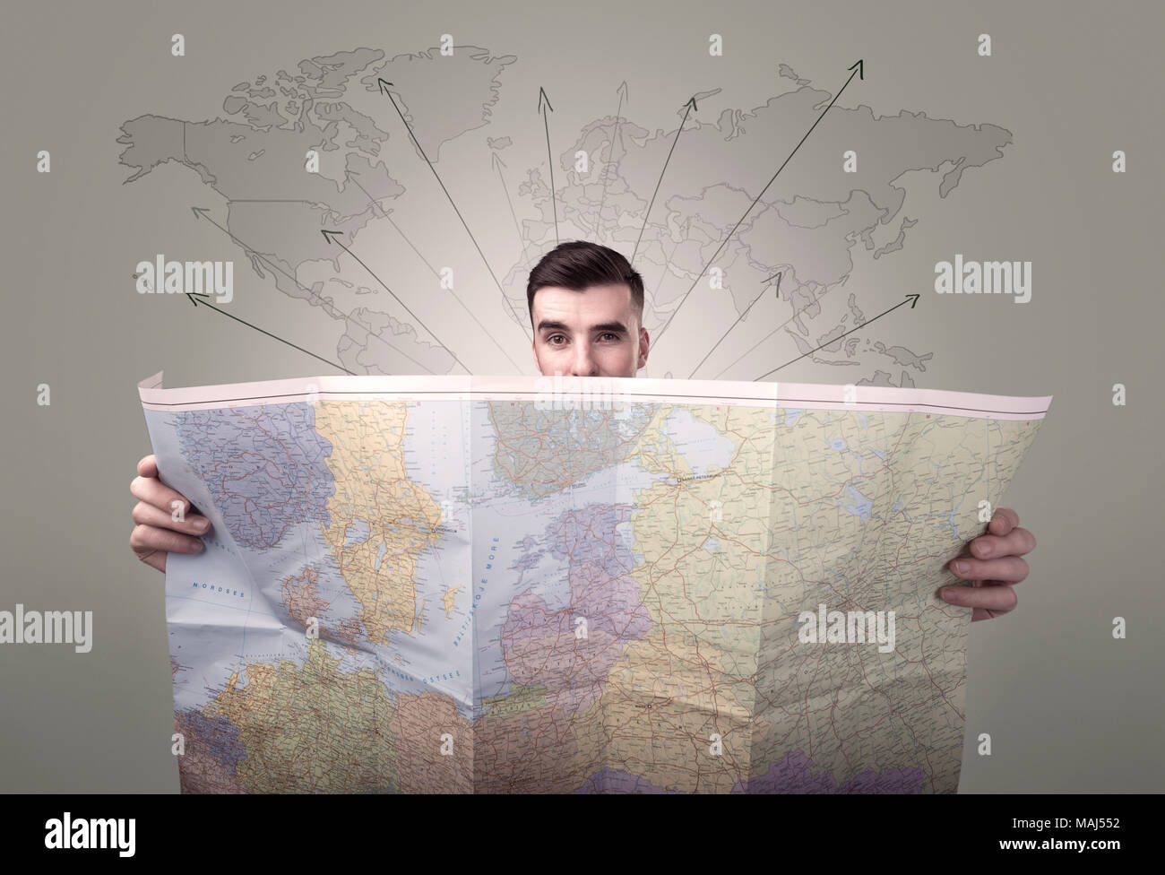 Handsome young man holding a map with world map and arrows behind him ...
