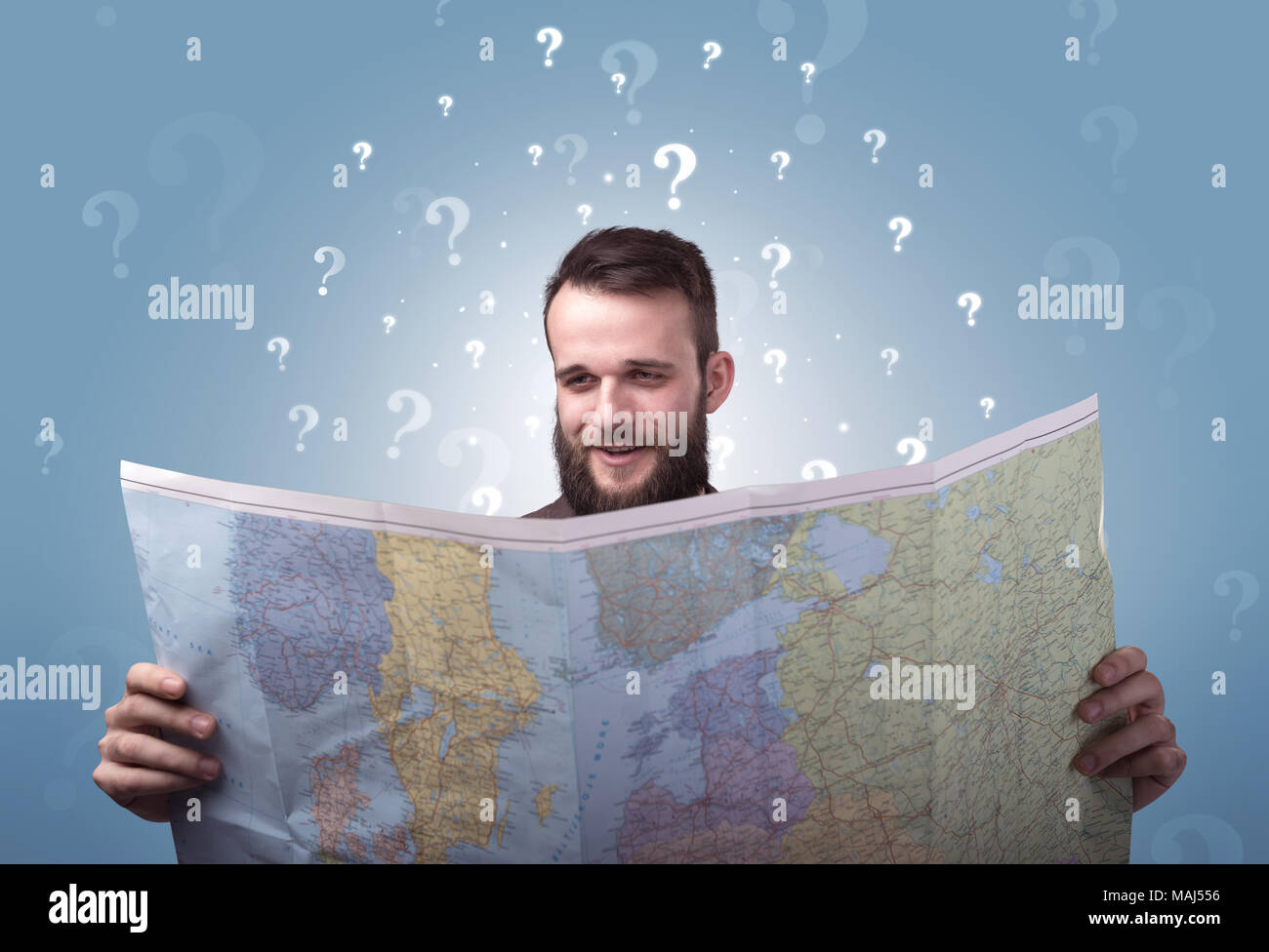 Handsome young man holding a map with white question marks above his ...