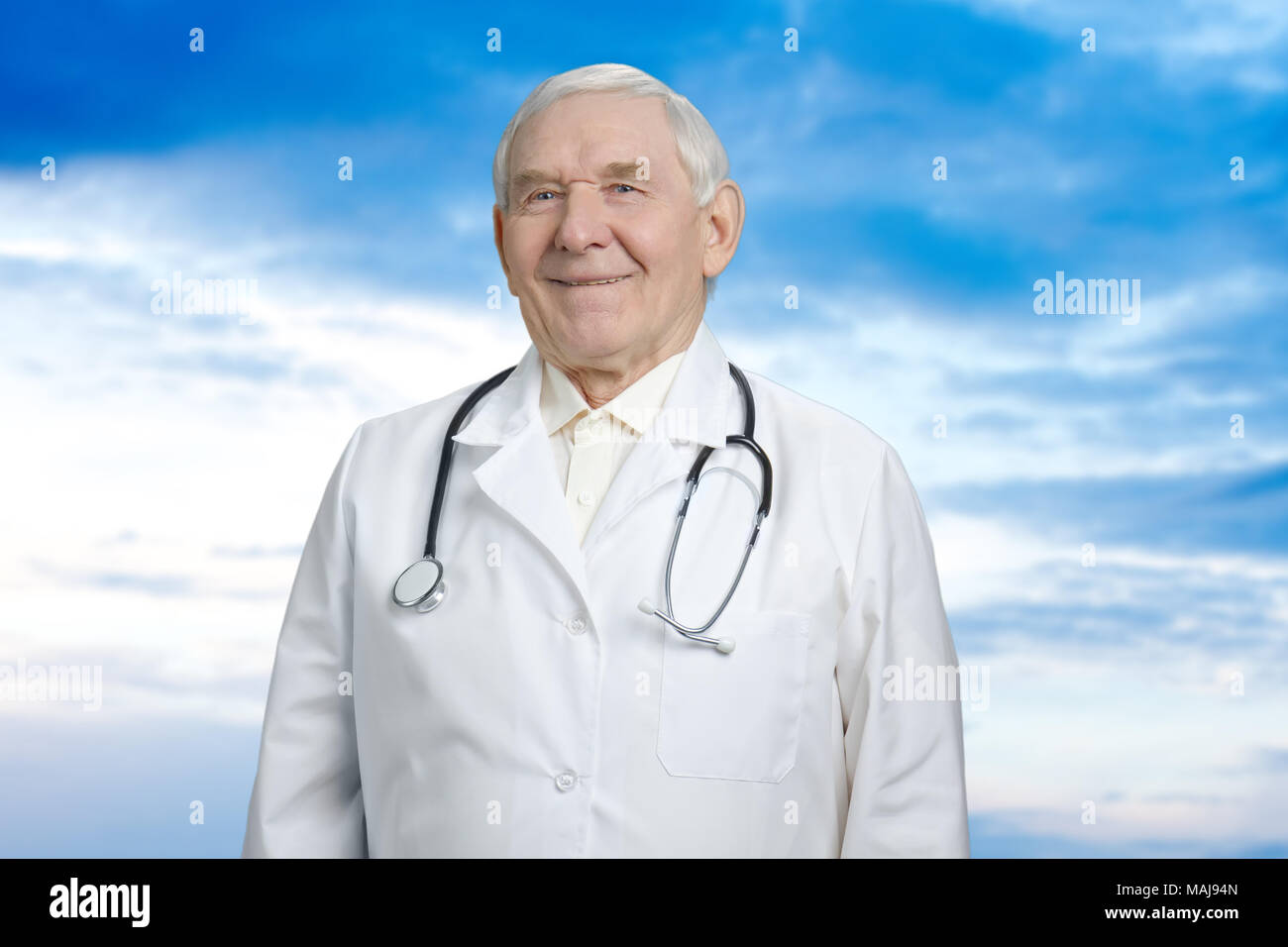Senior doctor against blue sky background. Smilng old man working as ...