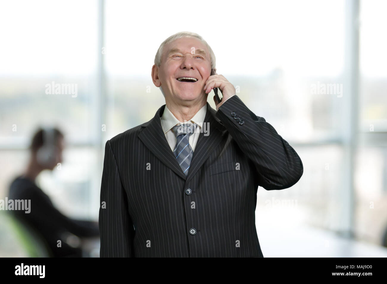 Happy cheerful businessman in suit talking on phone. Bright office ...