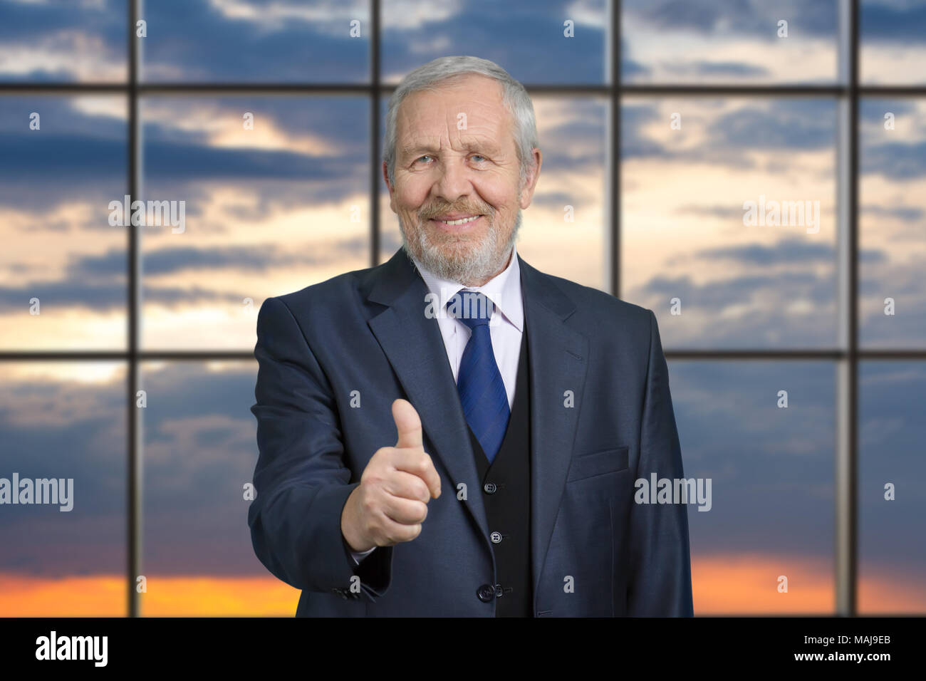 Portrait of old TV presenter with thumb up. Senior businessman in suit ...
