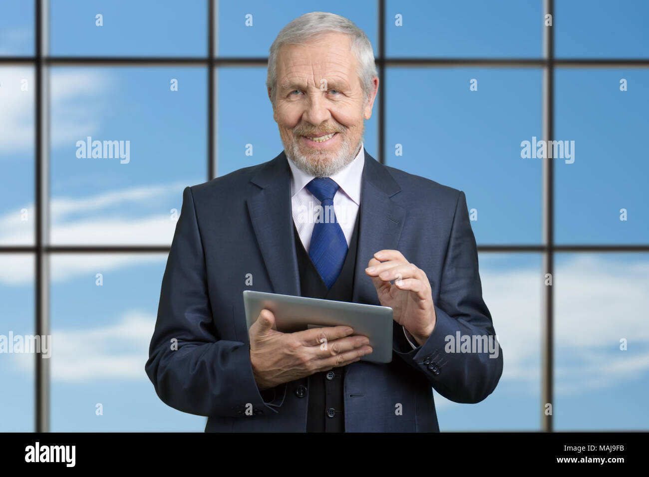 Portrait of happy old supervisor using tablet. Windows background with ...