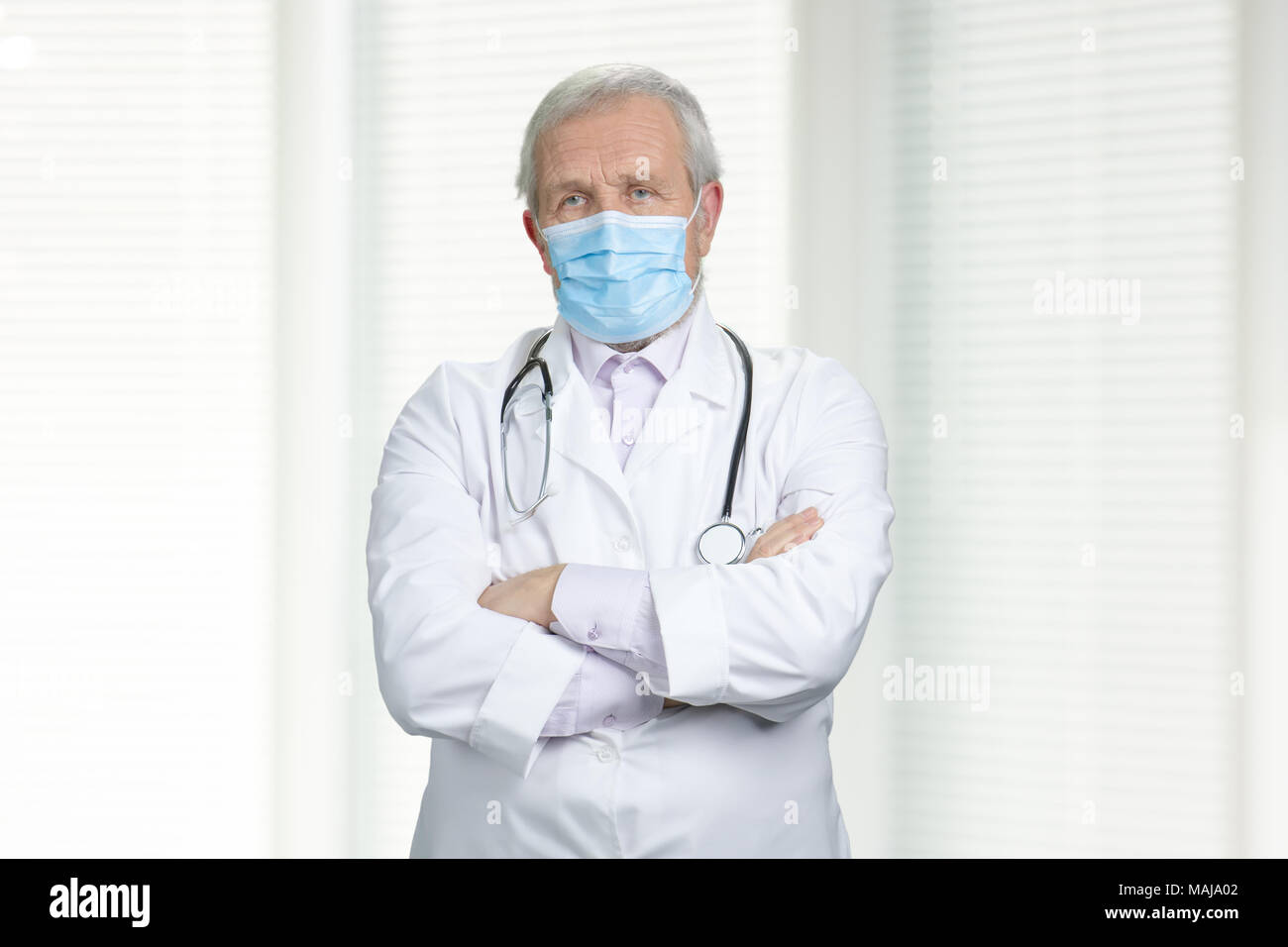 Serious old doctor with medical mask and folded arms. Portrait of ...
