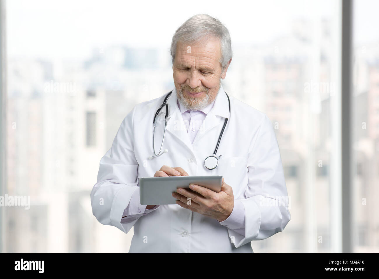 Old senior doctor tapping tablet. Portrait of physician using modern ...