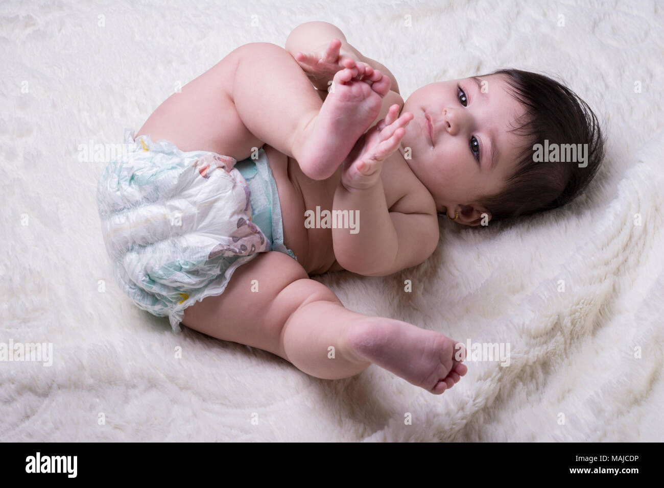 Little baby lying on white fluffy blanket and holding her leg Stock ...