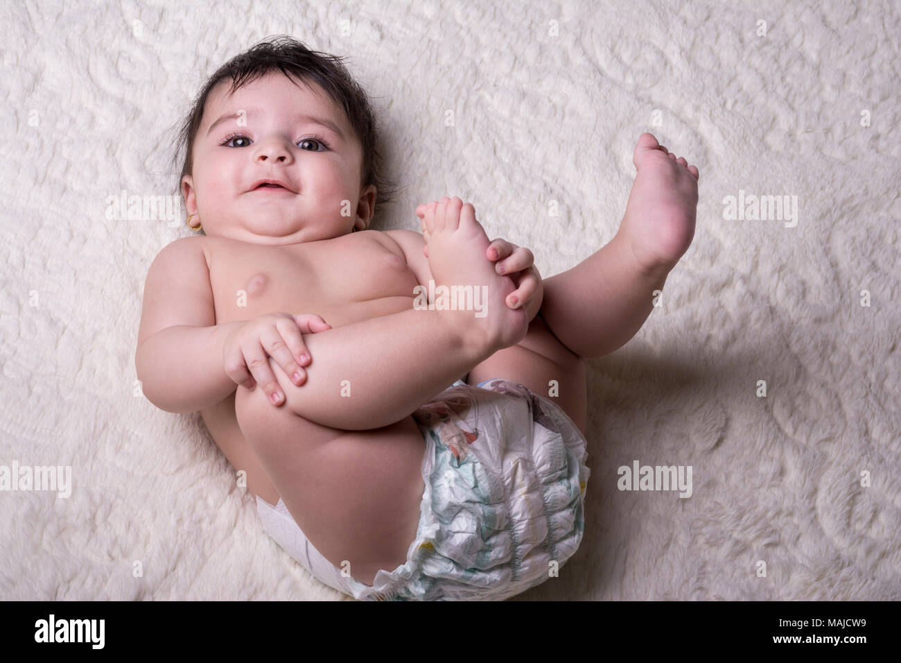 Little baby wearing a diaper playing on a white fluffy sheet and ...