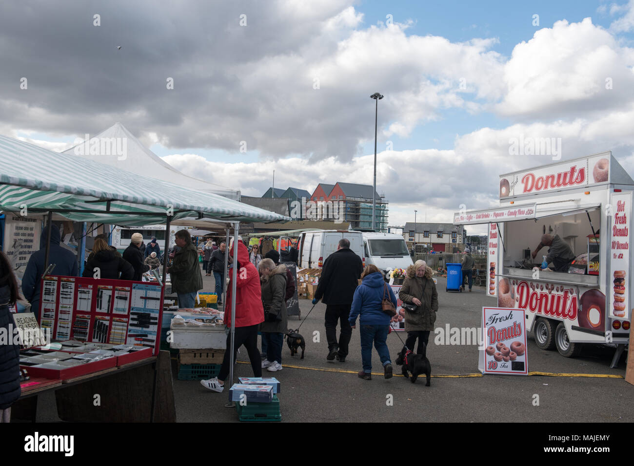 People browsing stalls and food vans at an outdoor market under cloudy ...