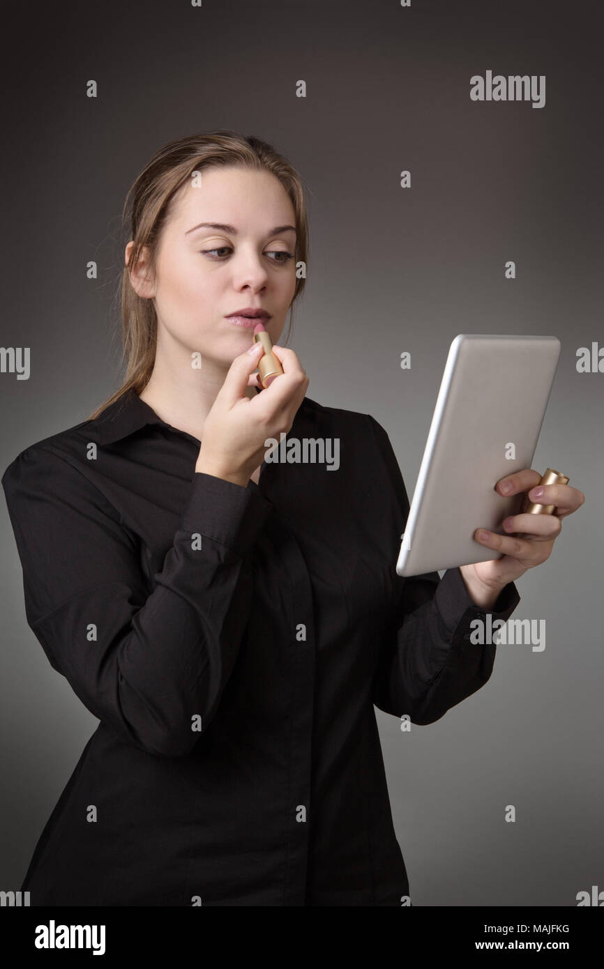 young business woman putting on lipstick using a tablet computer as a ...