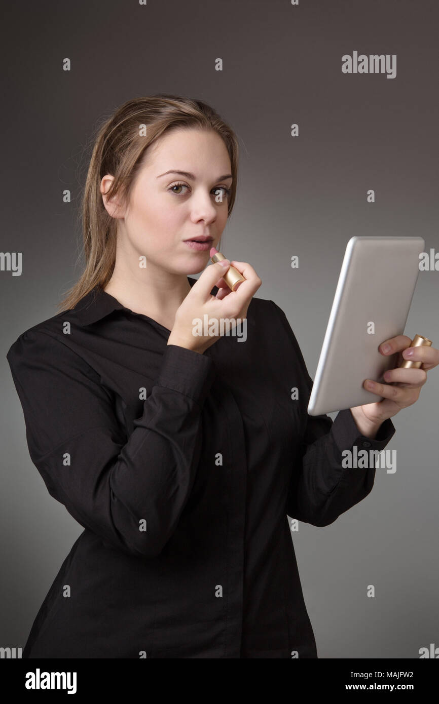 young business woman putting on lipstick using a tablet computer as a ...