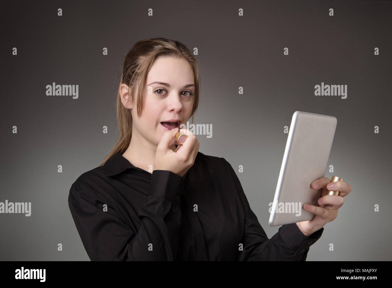 young business woman putting on lipstick using a tablet computer as a ...