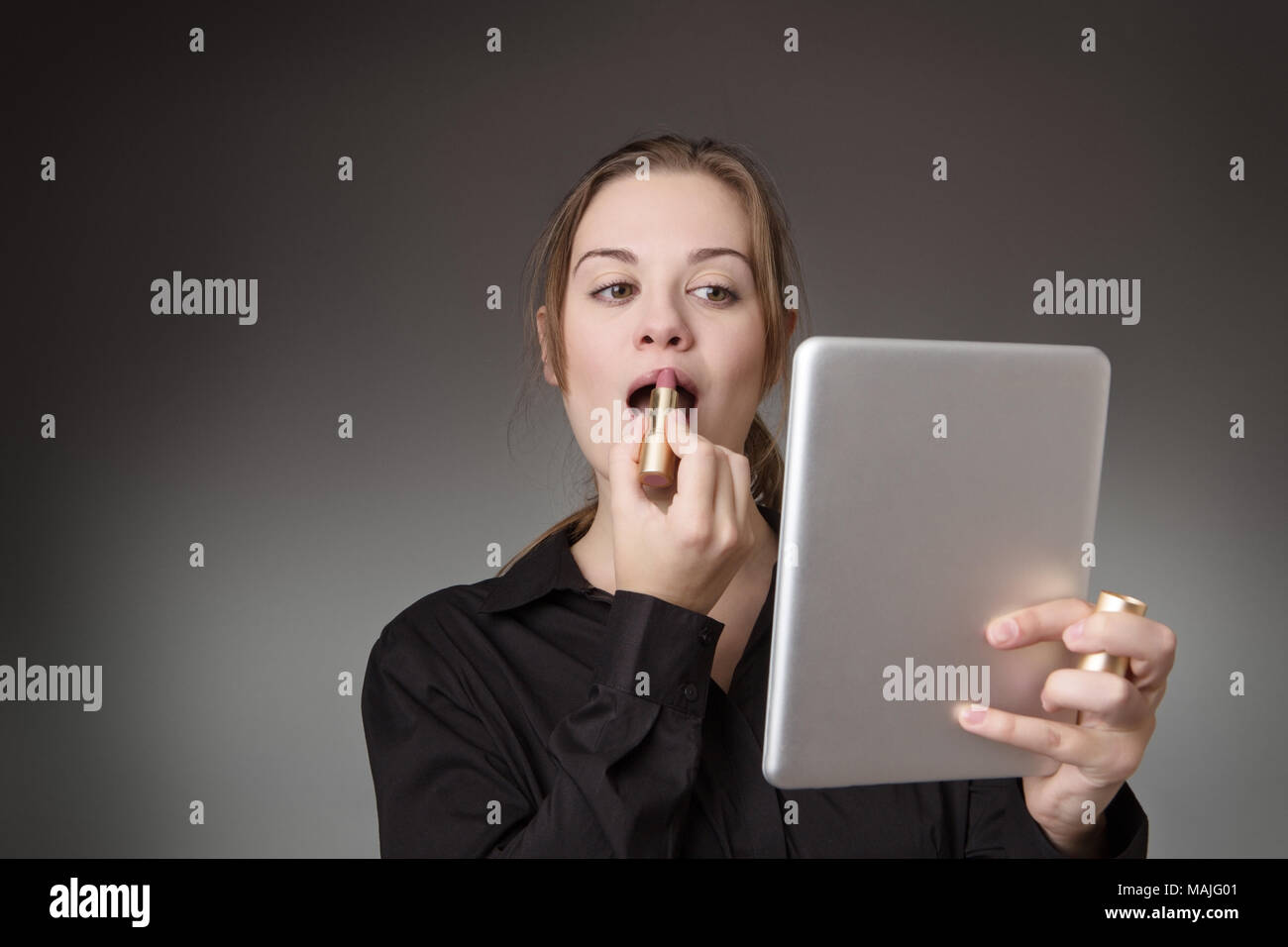 young business woman putting on lipstick using a tablet computer as a ...