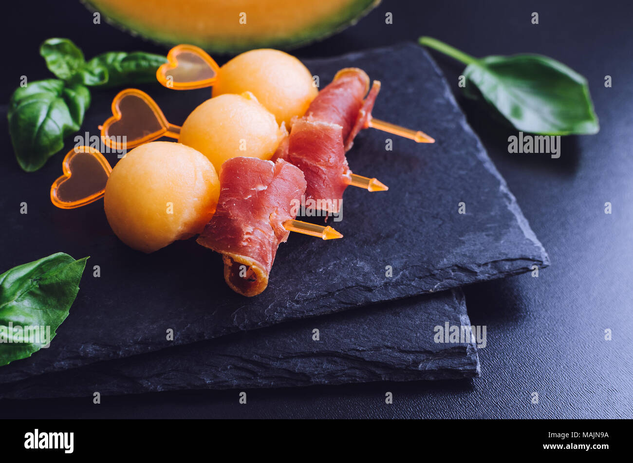 Colorful canape on skewers with melon and prosciutto on a slate plate ...