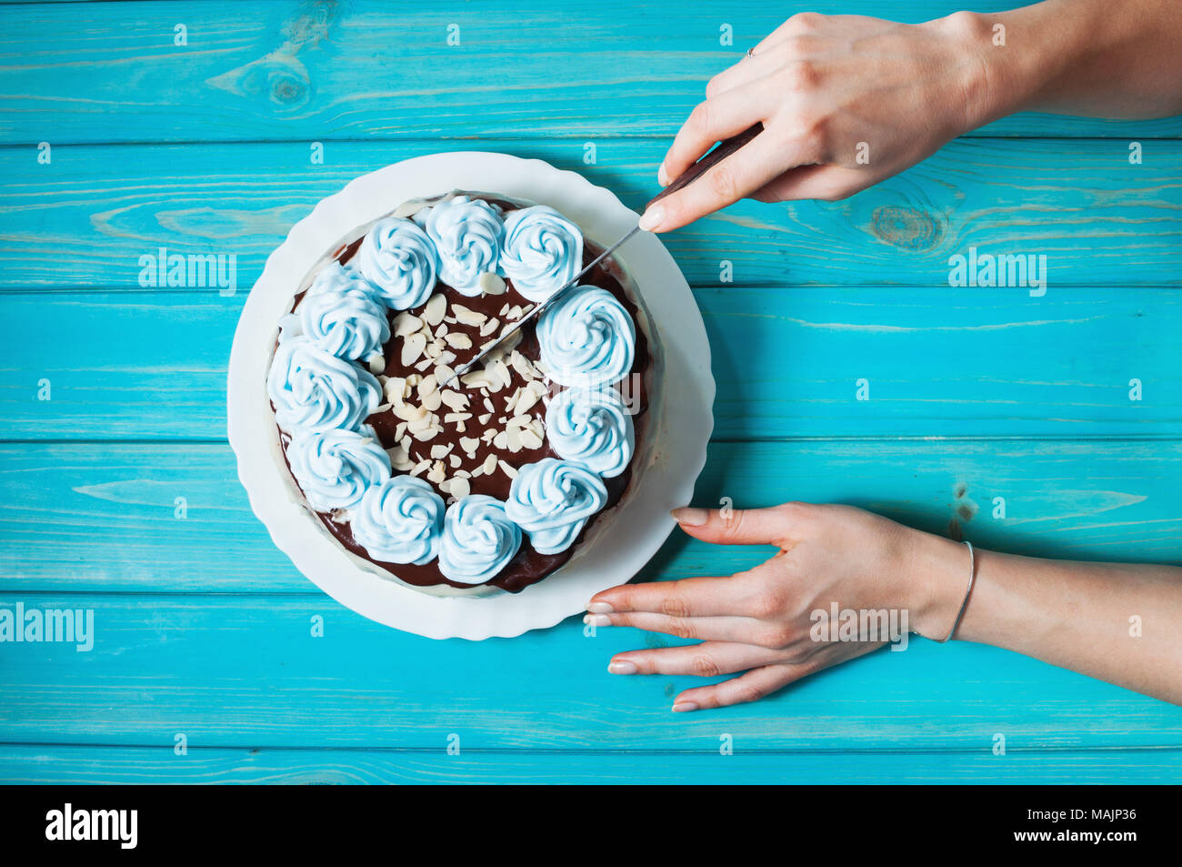 Woman's hands cut the cake with blue cream on blue wood background ...