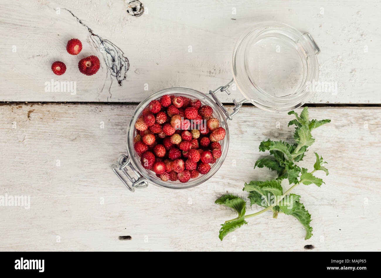 Wild strawberry in glass jar with green mint leaves on white rustic ...