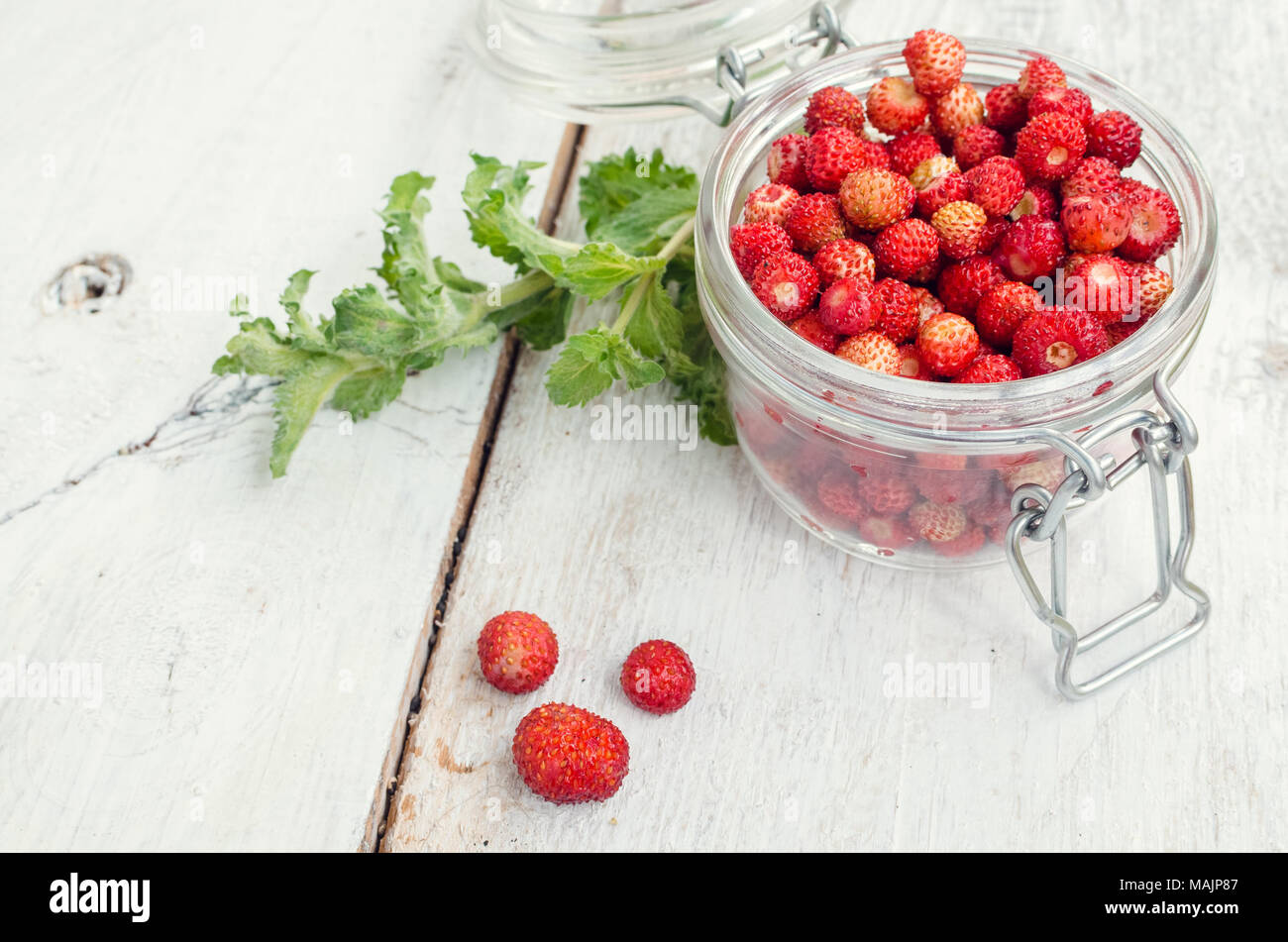 Wild strawberry in glass jar with green mint leaves on white rustic ...