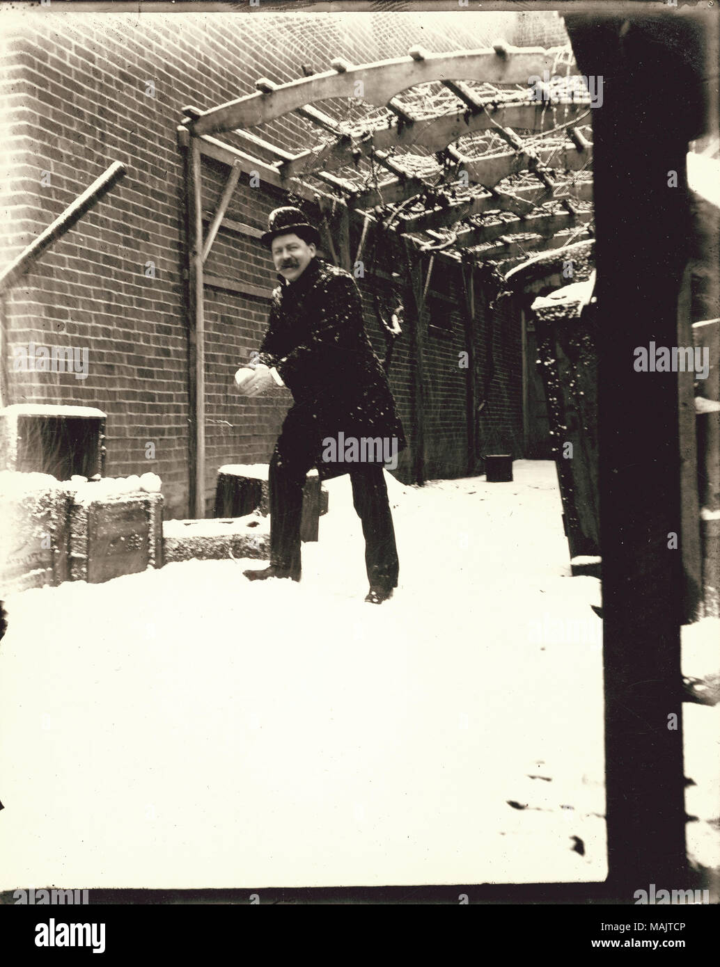 Title: Unidentified man making a snowball behind a brick building ...