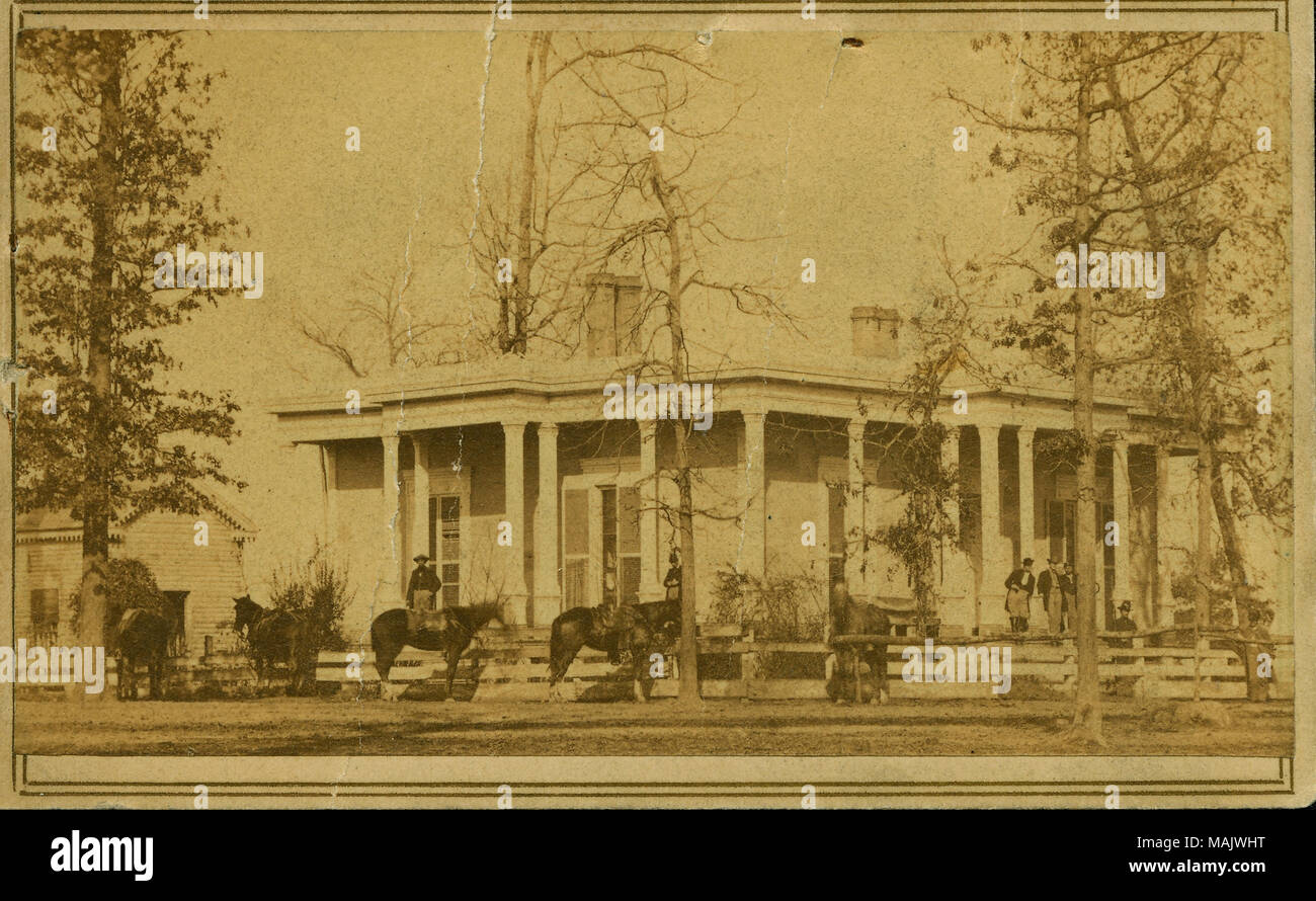 Photograph of a building with five horses hitched on fence and seven ...