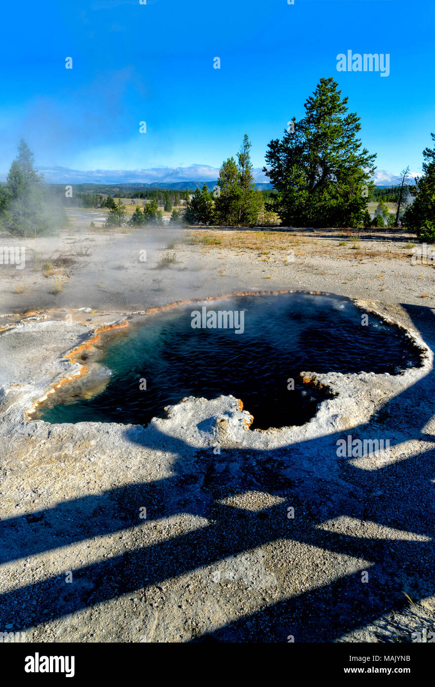 Shadow of fence on ground near hot spring with steam rising up off the ...