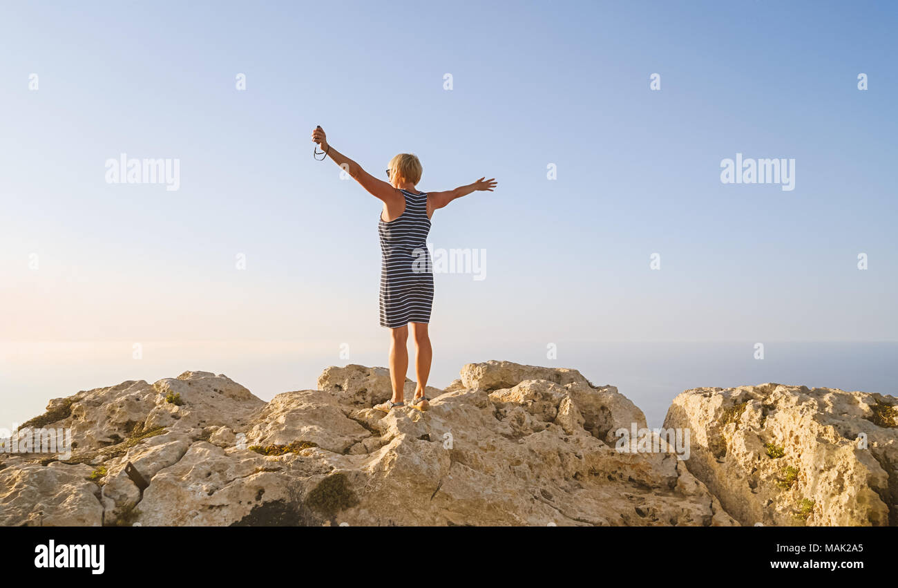 Happy middle-aged woman in blue dress greets the sun dawn and enjoying ...