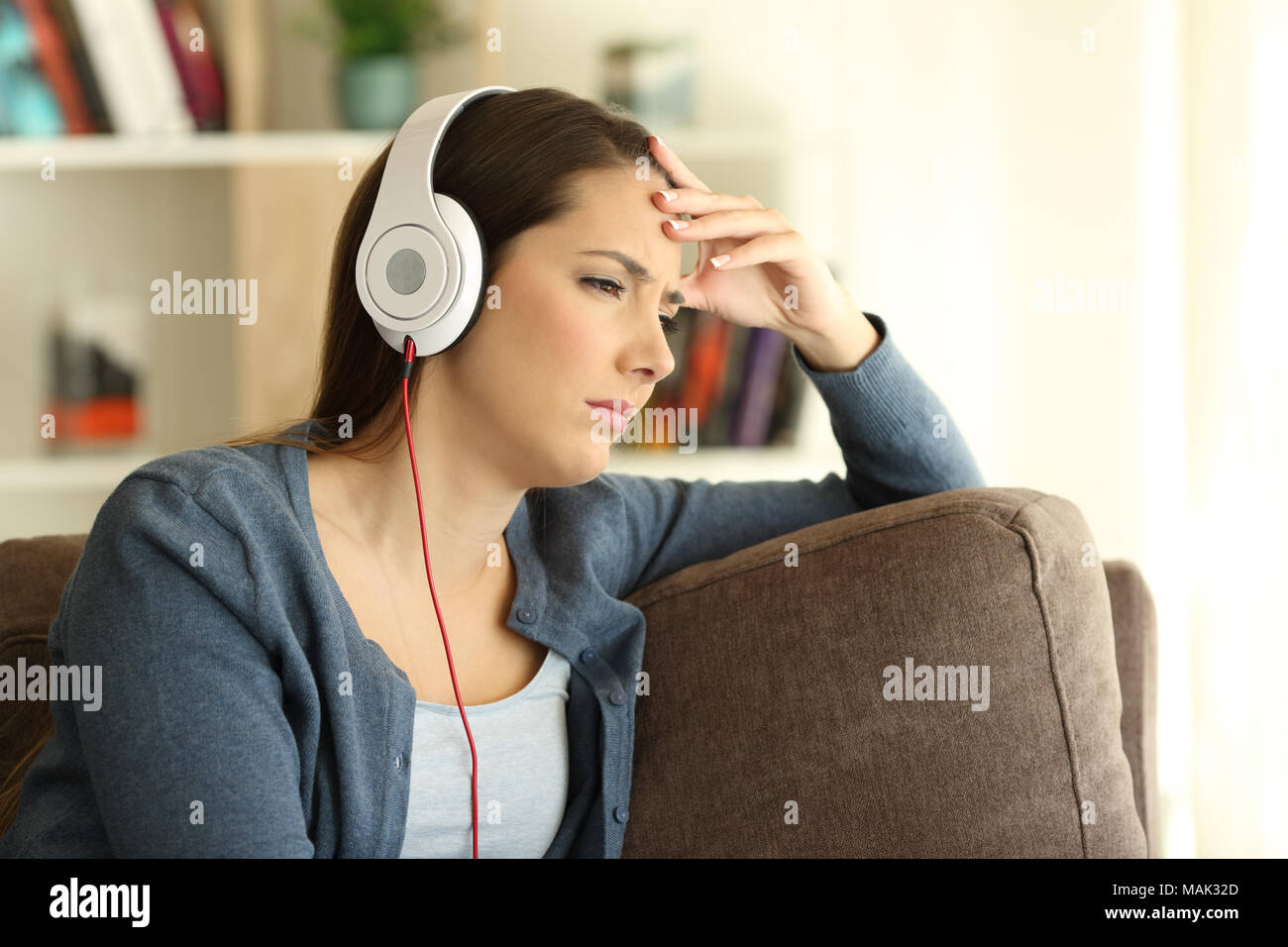 Worried girl listening to music sitting on a couch in the living room ...