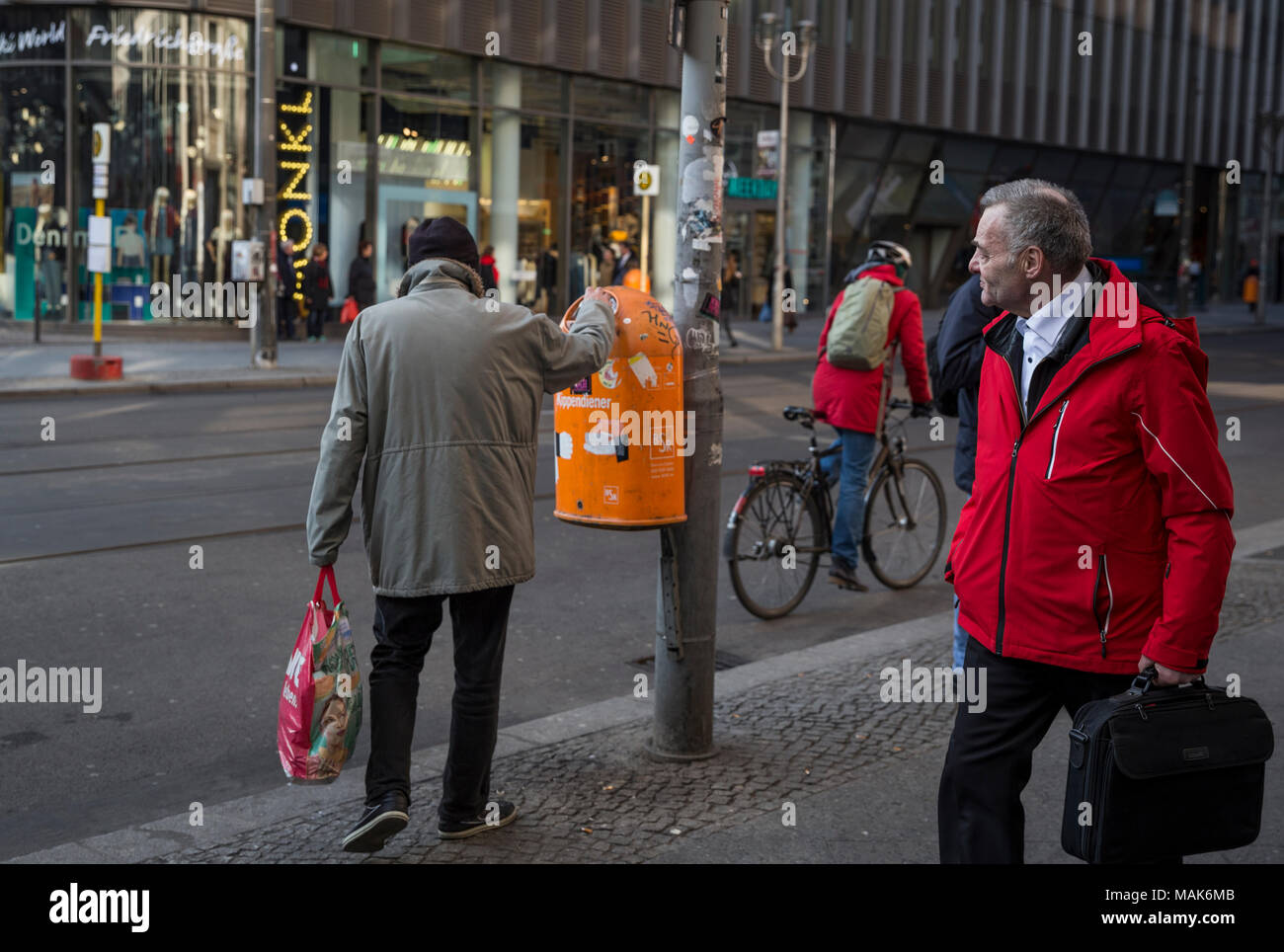 A pedestrian looks at a man taking something out of a bin in Berlin ...