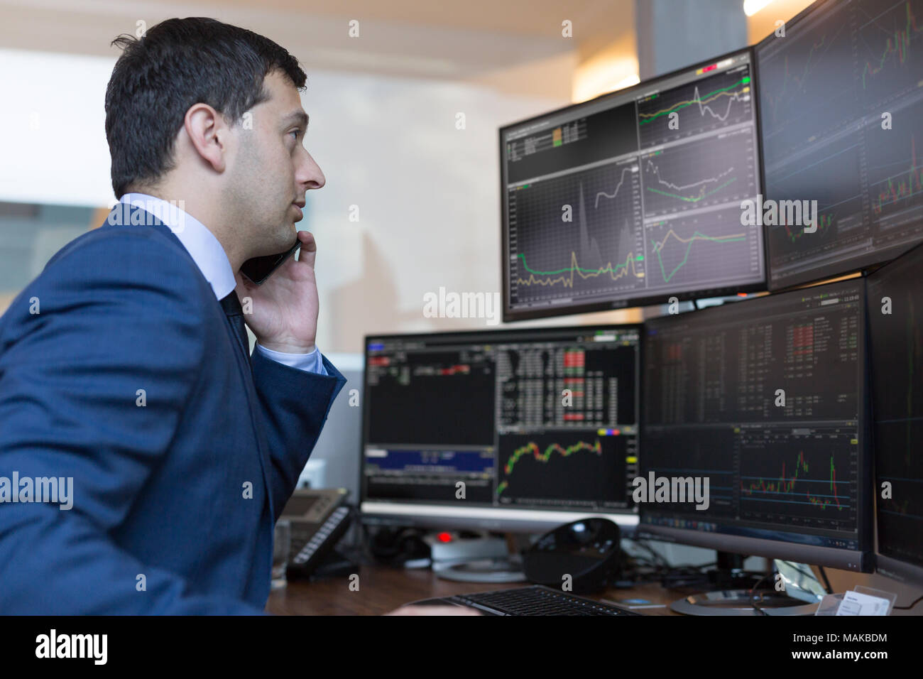 Stock broker trading online watching charts and data analyses on multiple computer screens Stock ...