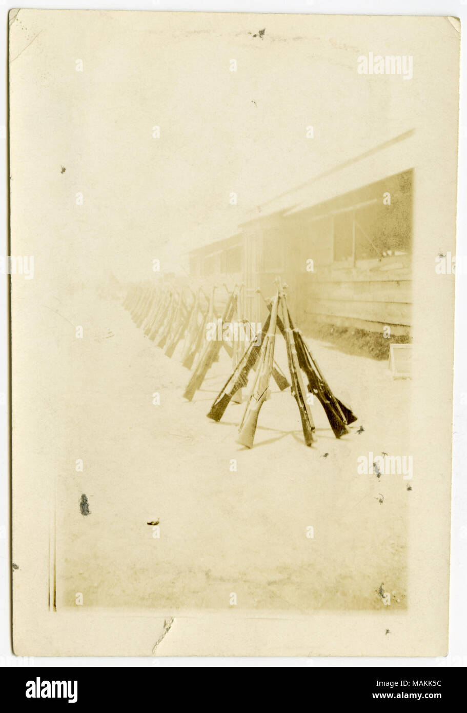 Vertical, sepia photograph showing a row of stacked rifles in front of ...