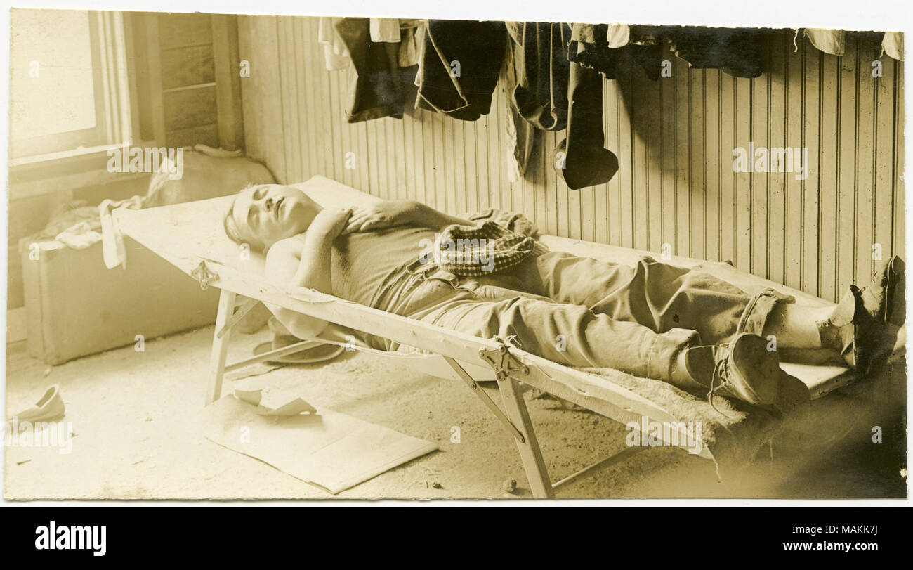 Horizontal, sepia photograph showing a man sleeping on a cot in a wood ...