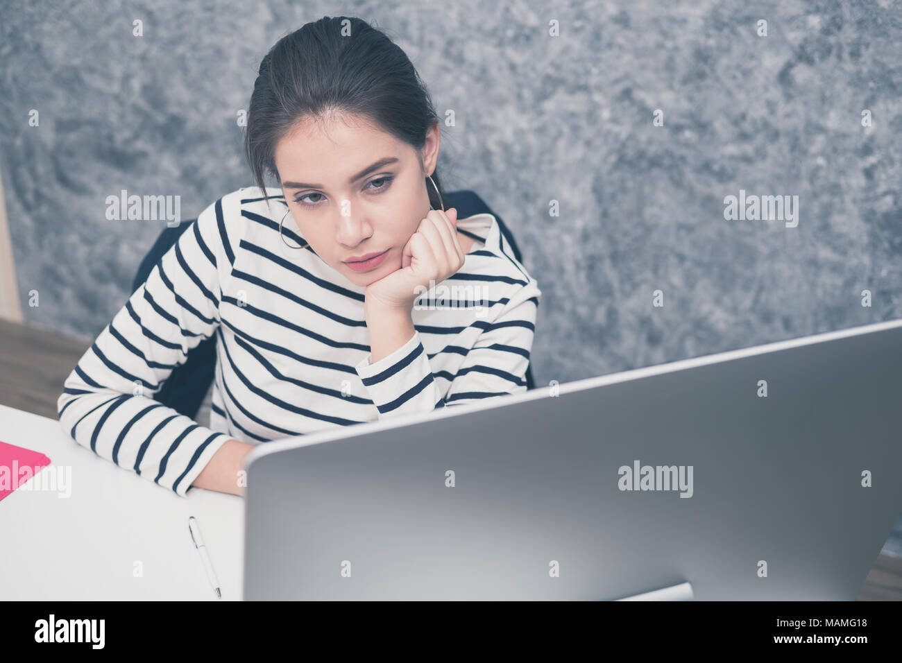 Beautiful young woman looking at a computer screen and thinking at the ...