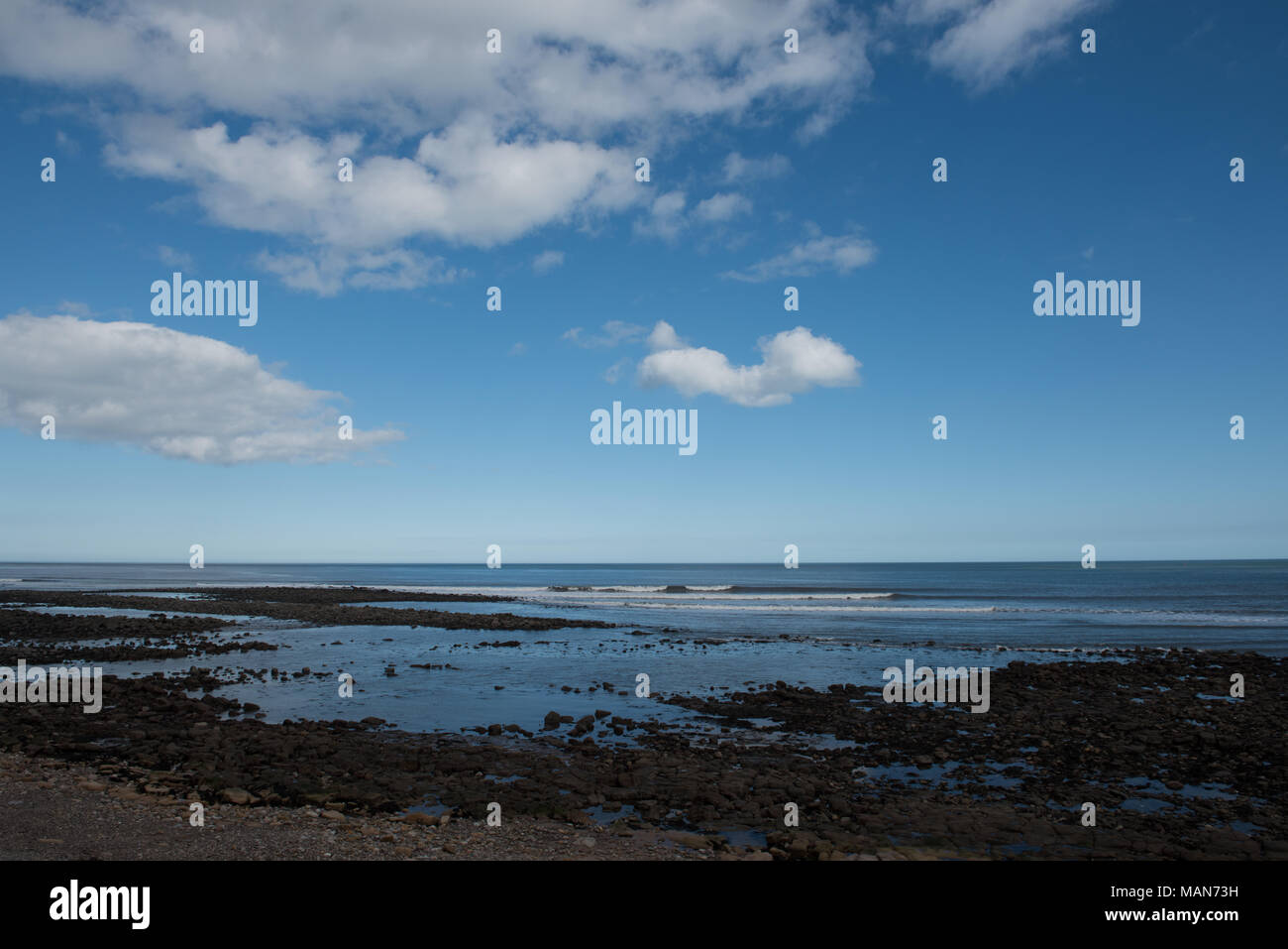 Rocky shoreline at low tide under a bright blue sky with scattered ...