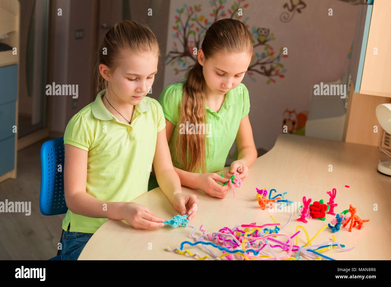 Cute little girls creating toys with chenille sticks at the table ...