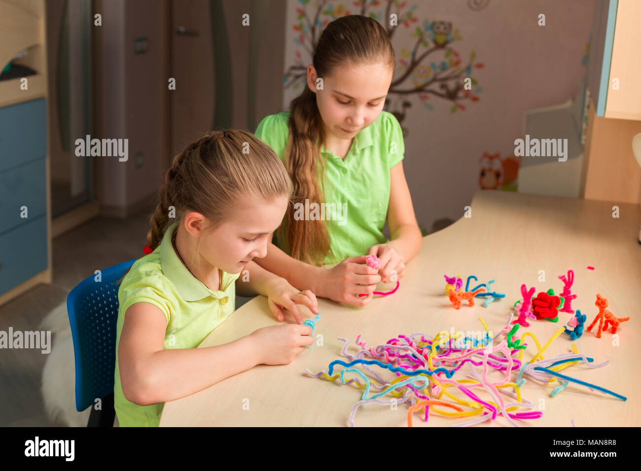 Cute little girls creating toys with chenille sticks at the table ...