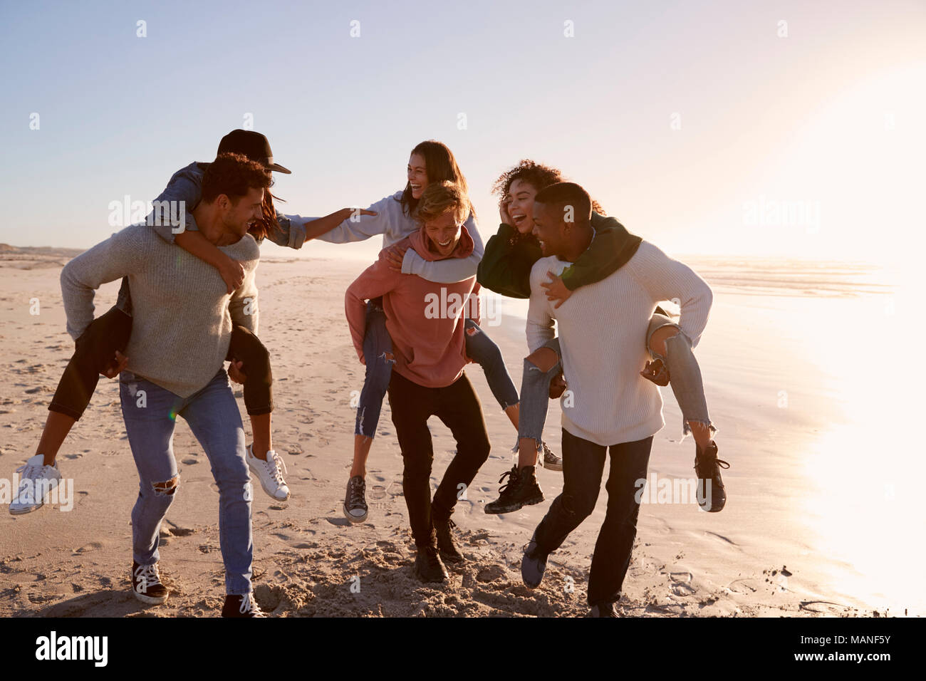 Group Of Friends Having Piggyback Race On Winter Beach Together Stock ...