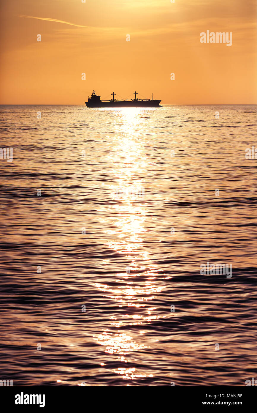 Sun setting at the sea with sailing cargo ship, scenic view Stock Photo ...