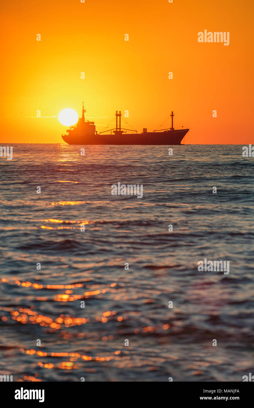 Sun setting at the sea with sailing cargo ship, scenic view Stock Photo ...