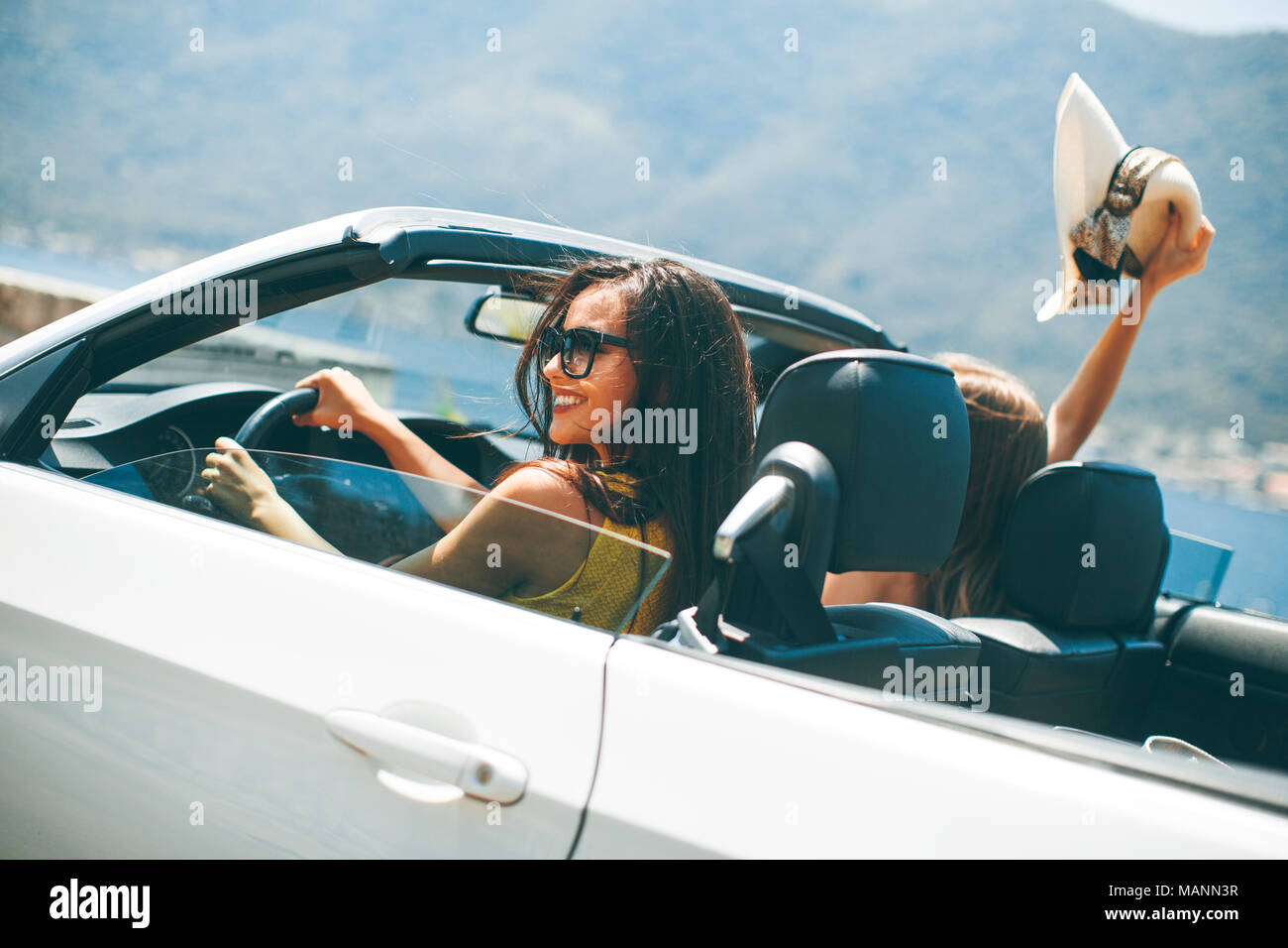 Two happy friends in white cabriolet car driving everywhere and looking ...