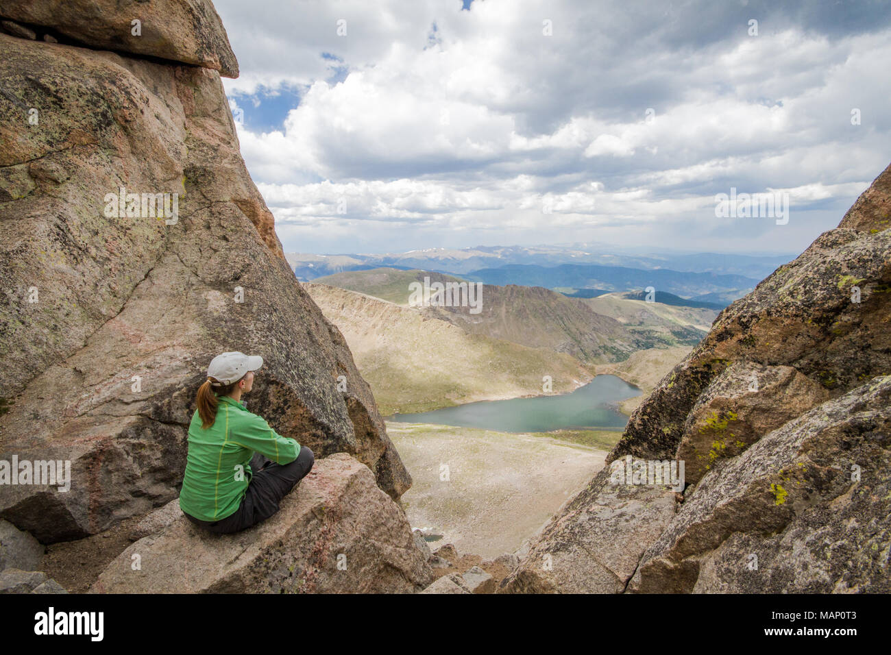 A female hike takes in the vista of surrounding mountains and alpine ...