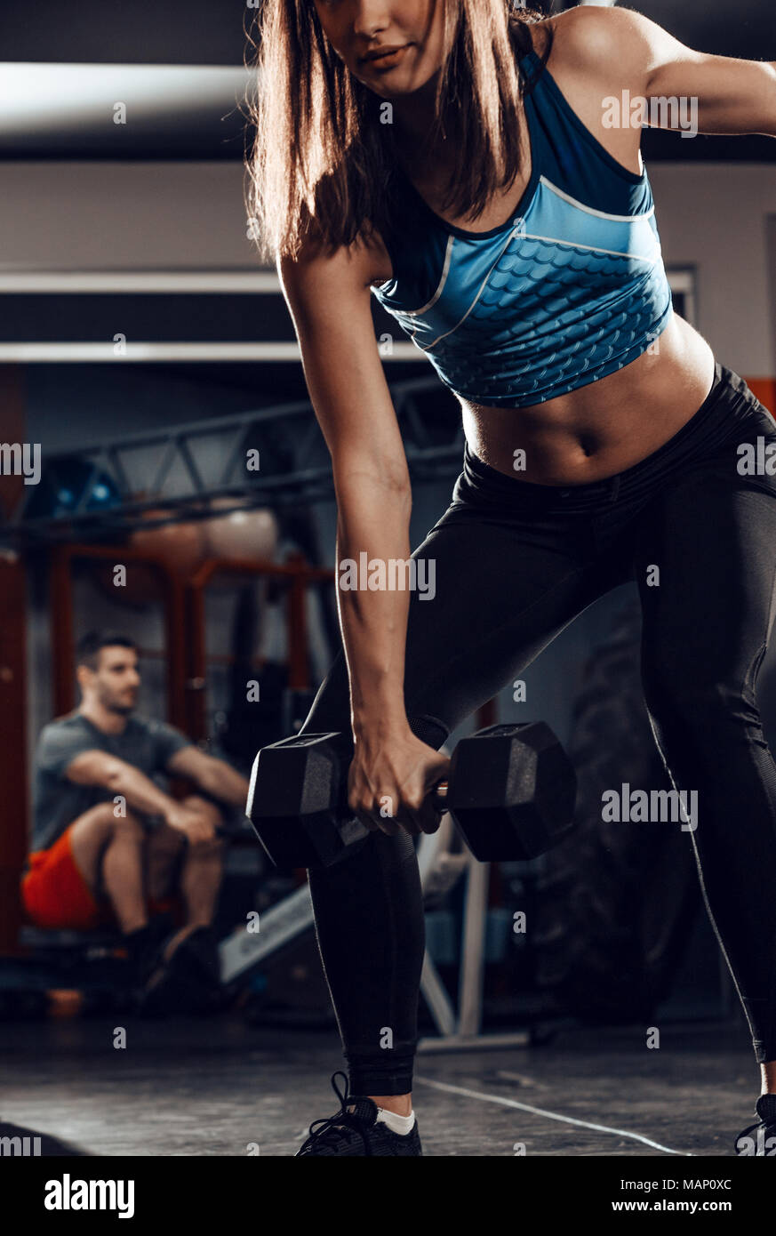 Young muscular cute woman doing hard exercise with dumbbell at the gym ...
