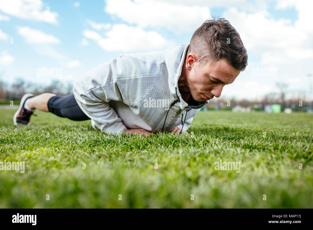 Young man athlete doing push ups and doing exercises on the green grass ...