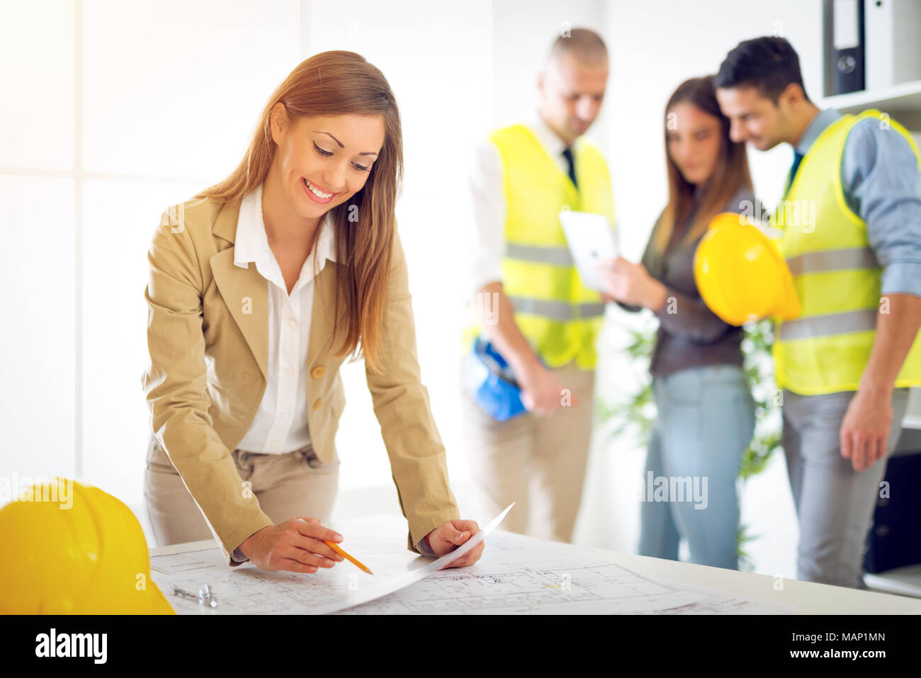 Smiling young woman constructor analyzing blueprint at desk in the ...
