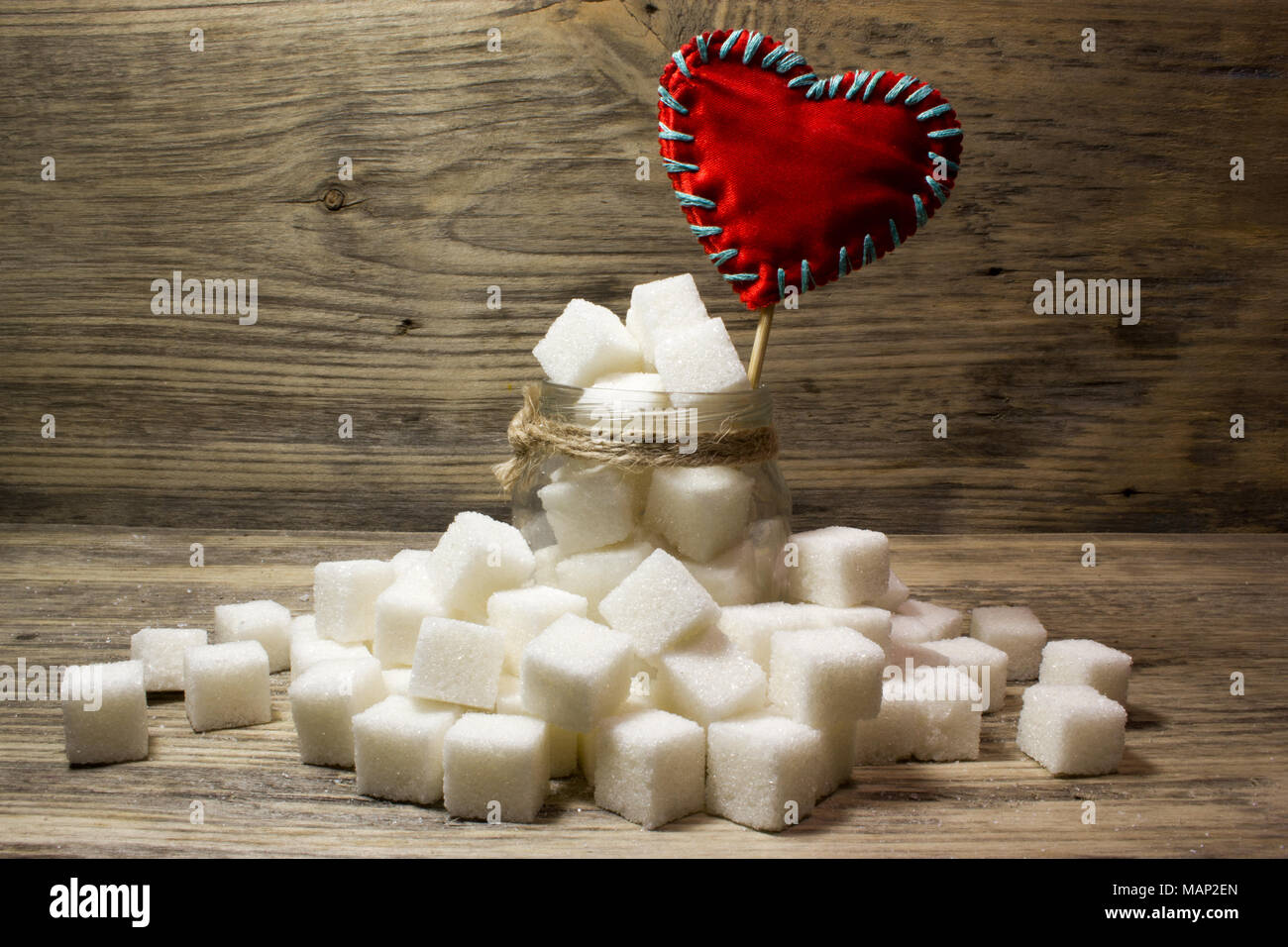 Sugar cubes and a red love heart in glass jar on wooden background ...