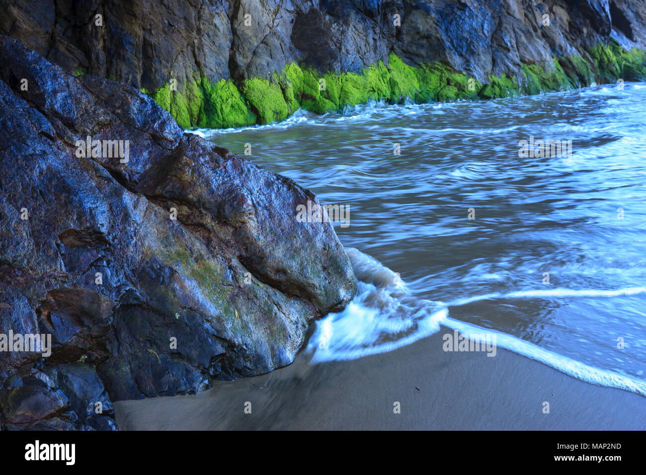 Water rushes up onto the beach by a rock wall on Hug Point park in ...