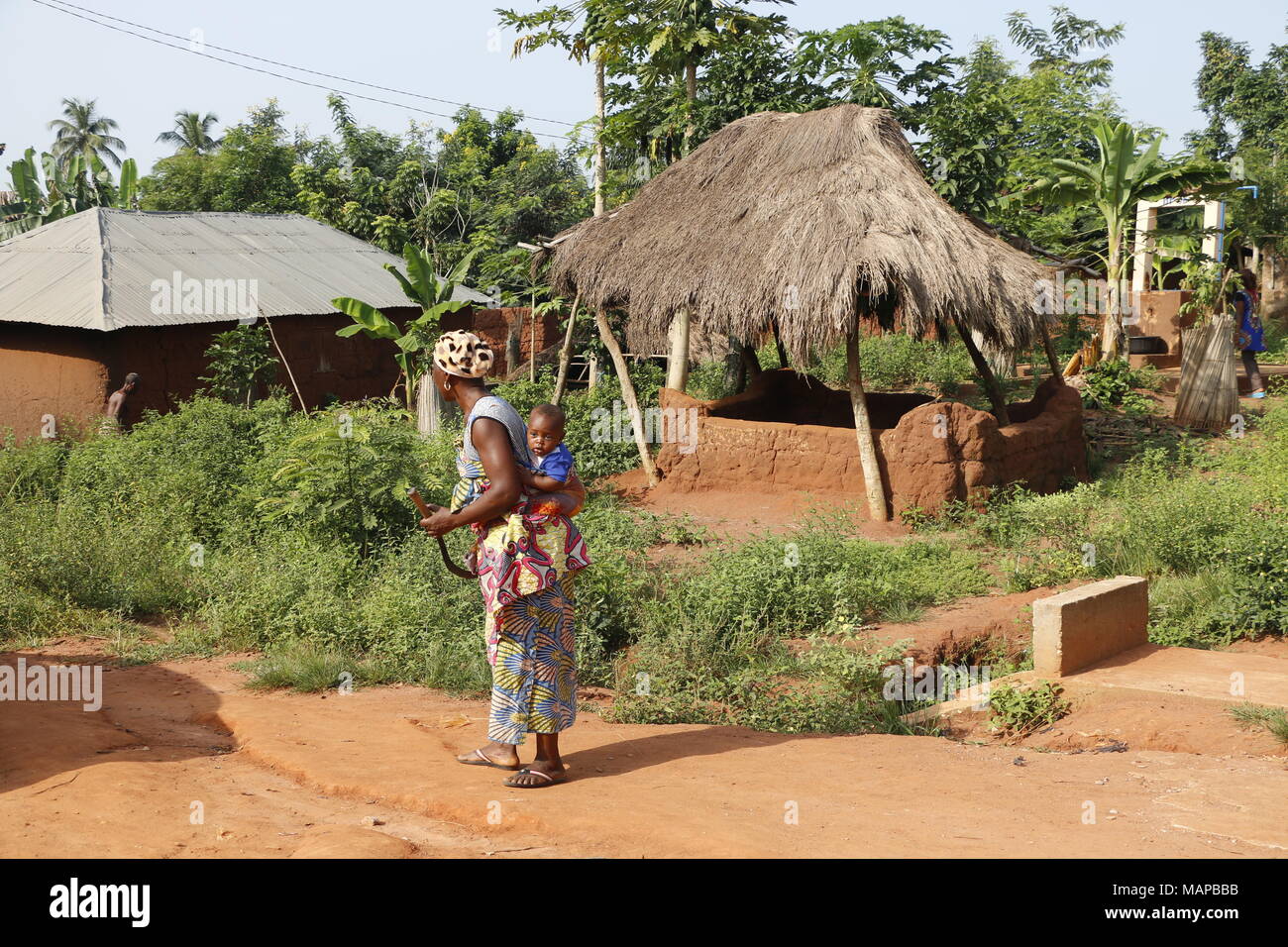Village life in Benin woman with a tool in her hand and a baby at her ...