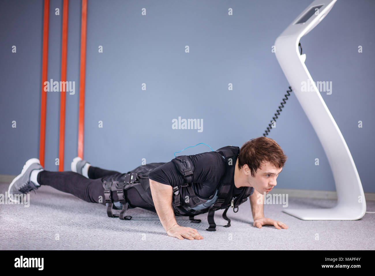 EMS male doing push ups in gym while connected to electric muscle ...