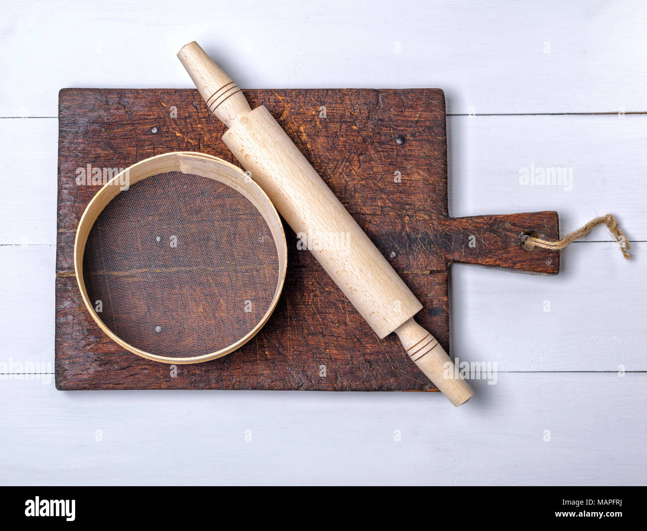 brown wooden kitchen cutting board, rolling pin and sieve on a white ...