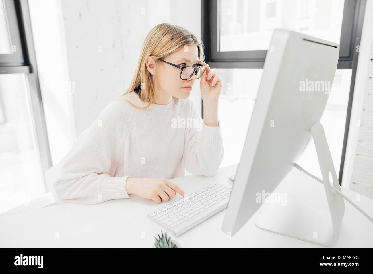 woman working in office, sitting at desk, using computer and looking on ...